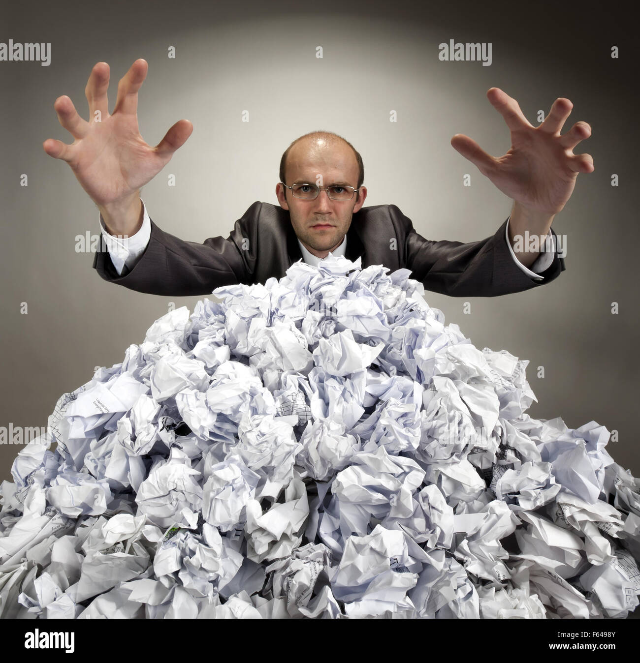 Serious businessman with raised hands reaches out from big heap of ...