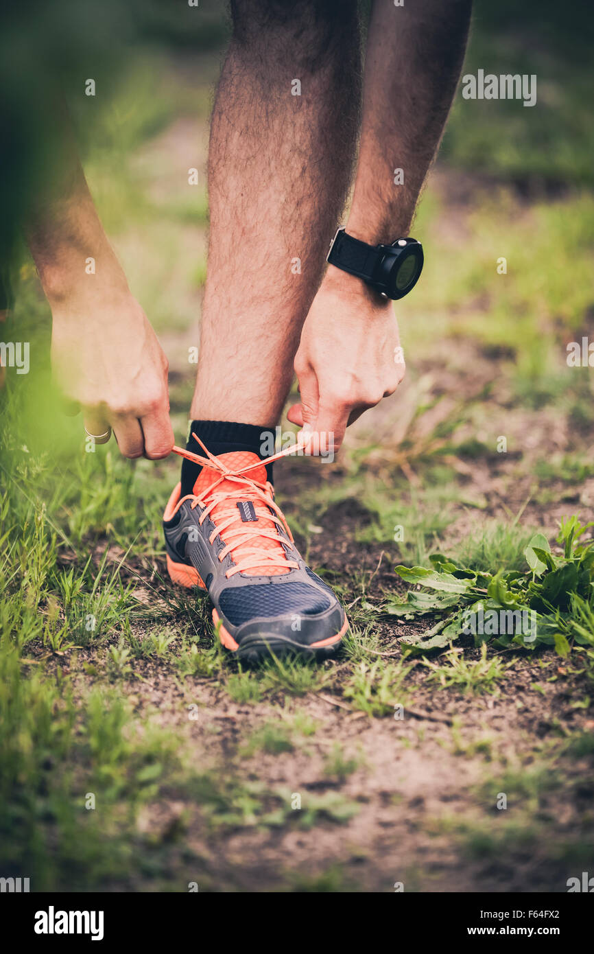 Runner tying sports shoe. Man running on cross country path in summer ...