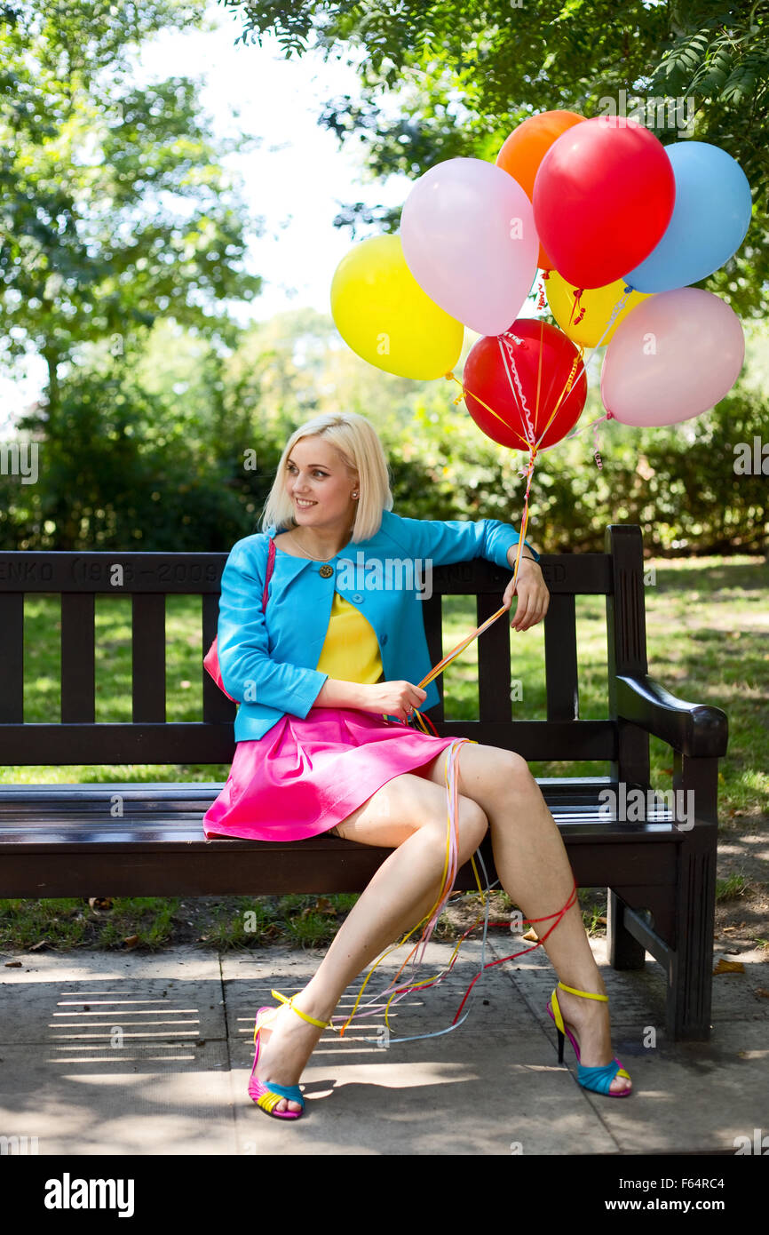 young woman sitting on a park bench holding a bunch of balloons Stock ...