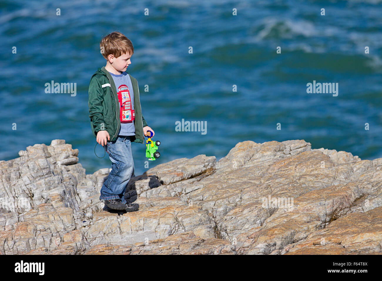 Young boy walking along rocks by the ocean Stock Photo - Alamy