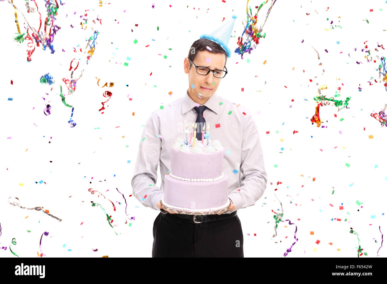Sad young man holding a birthday cake and crying with confetti ...