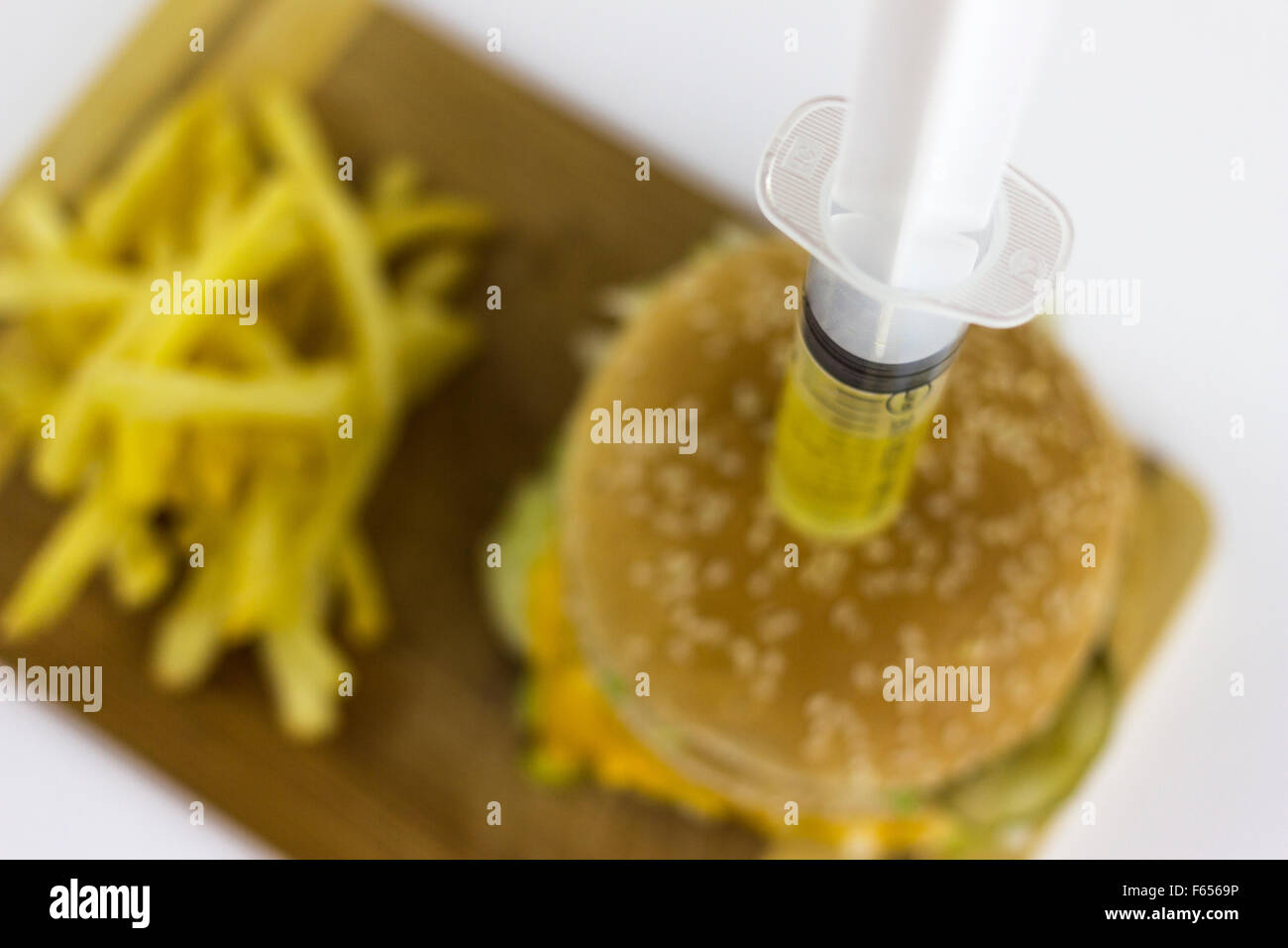 Syringe puming yellow liquid in a hamburger, on a white background ...