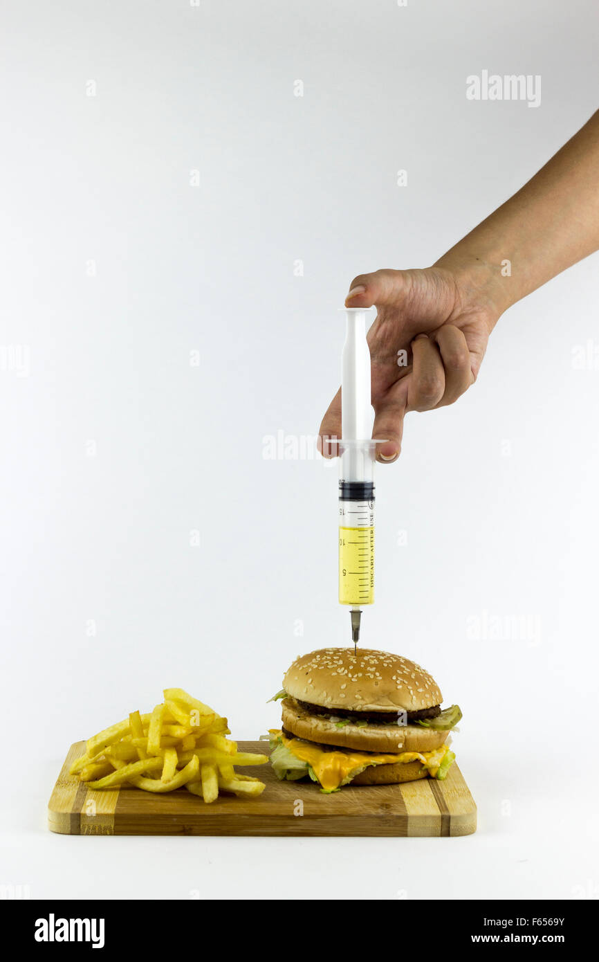 Hand pumping liquid in a hamburger with a syringe, on a white ...