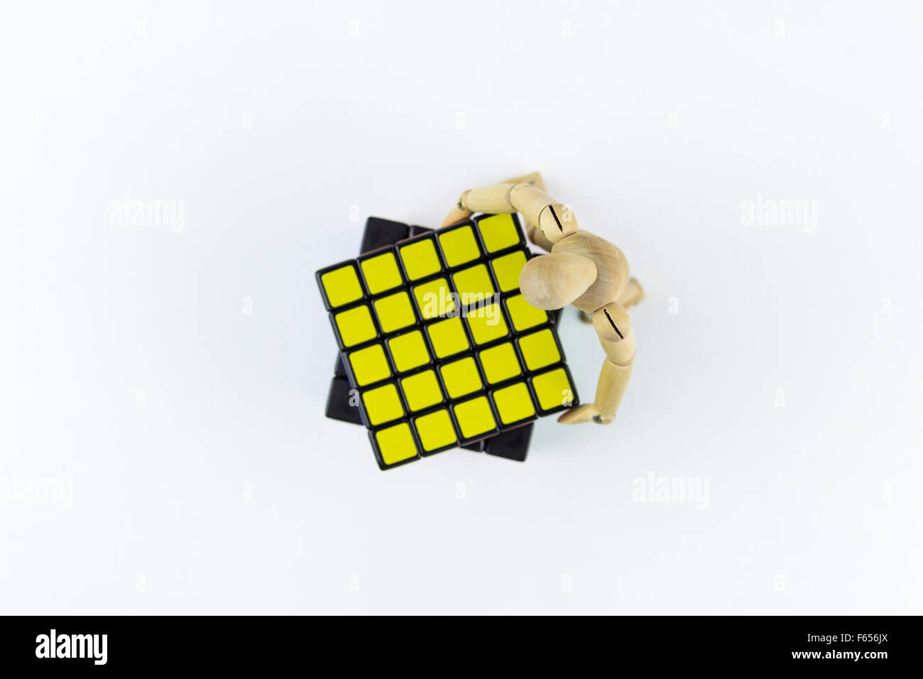 Wooden puppet trying to solve a puzzle cube, on a white background ...