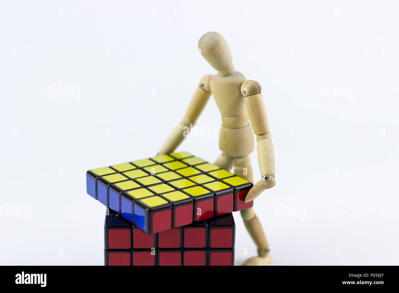 Wooden puppet trying to solve a puzzle cube, on a white background ...