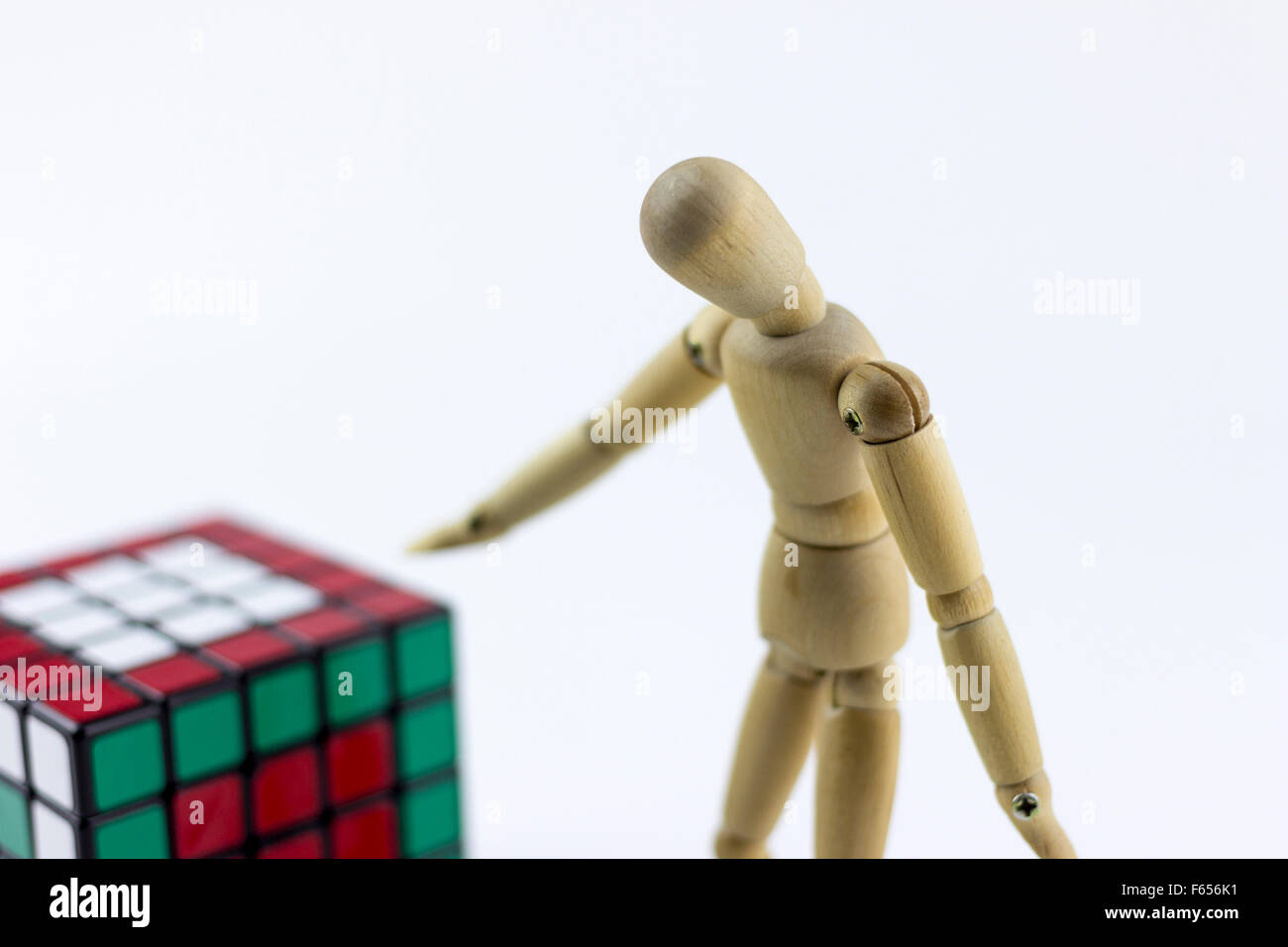 Wooden puppet trying to solve a puzzle cube, on a white background ...