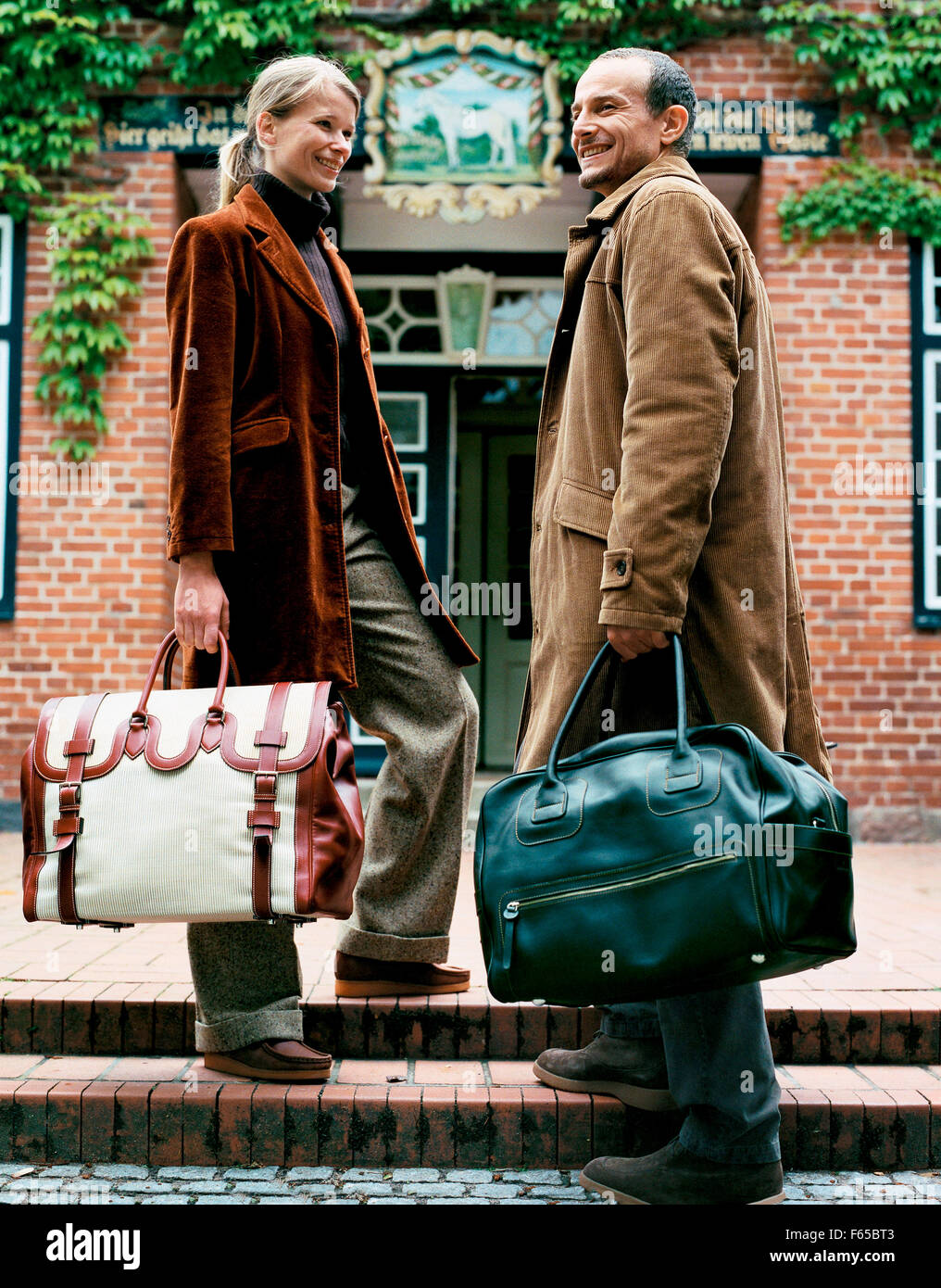 Couple wearing long coat holding travel bags in front of Ole Liese ...