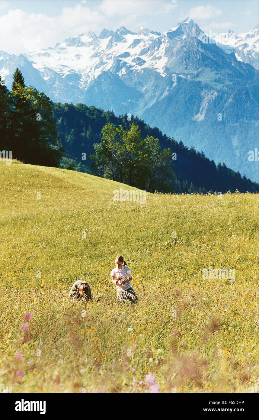 Children walking in meadow with snow-capped mountains in background ...