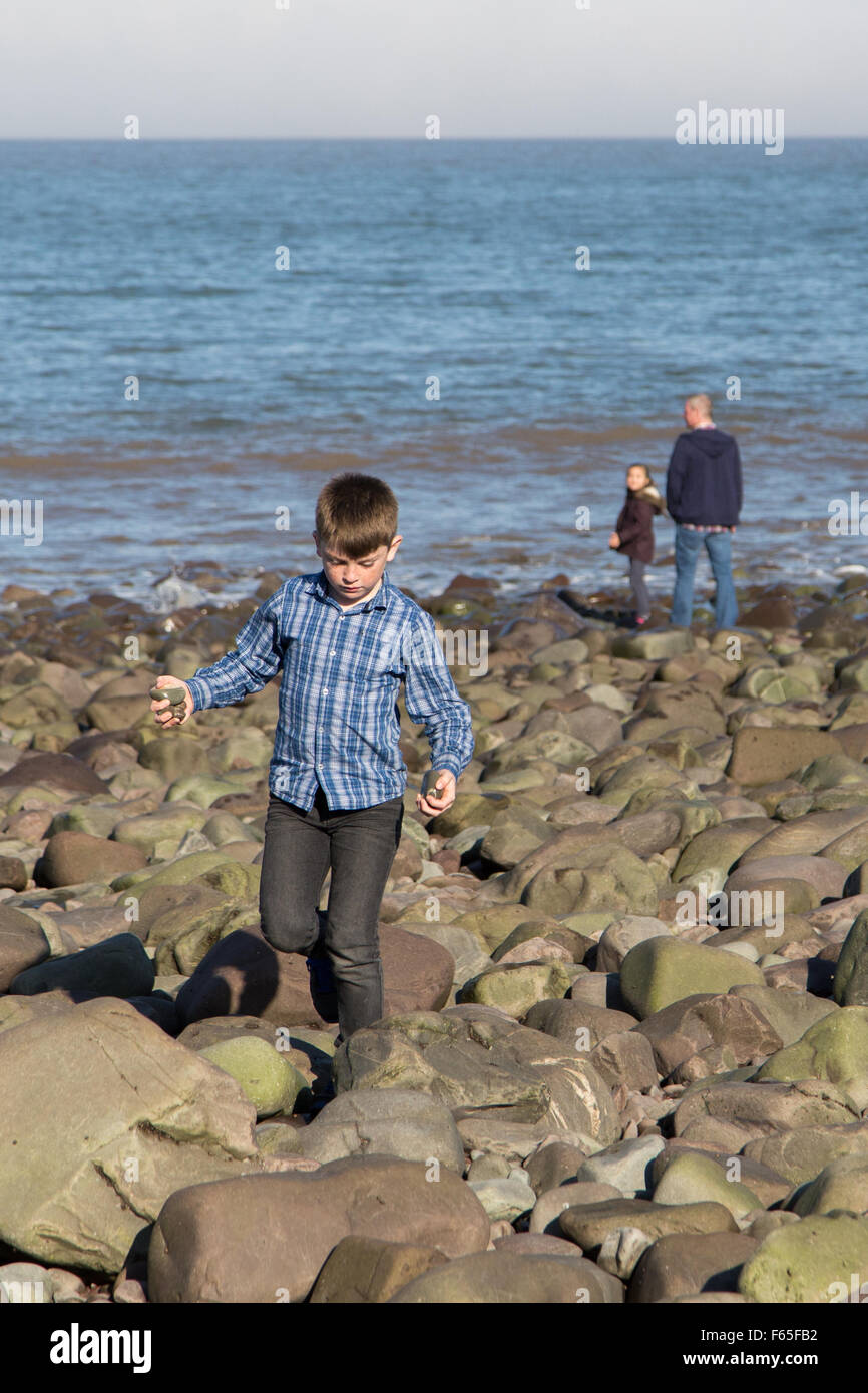 A young boy walk over rocks, fossil hunting at Porlock Weir coastline ...