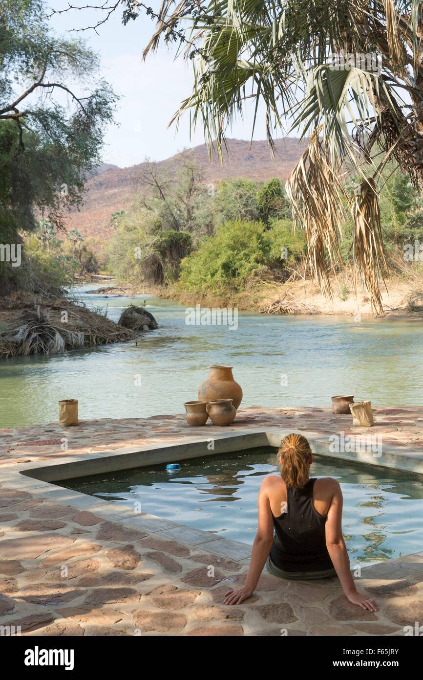 A woman sitting at a pool on the Kunene River, border between Namibia ...