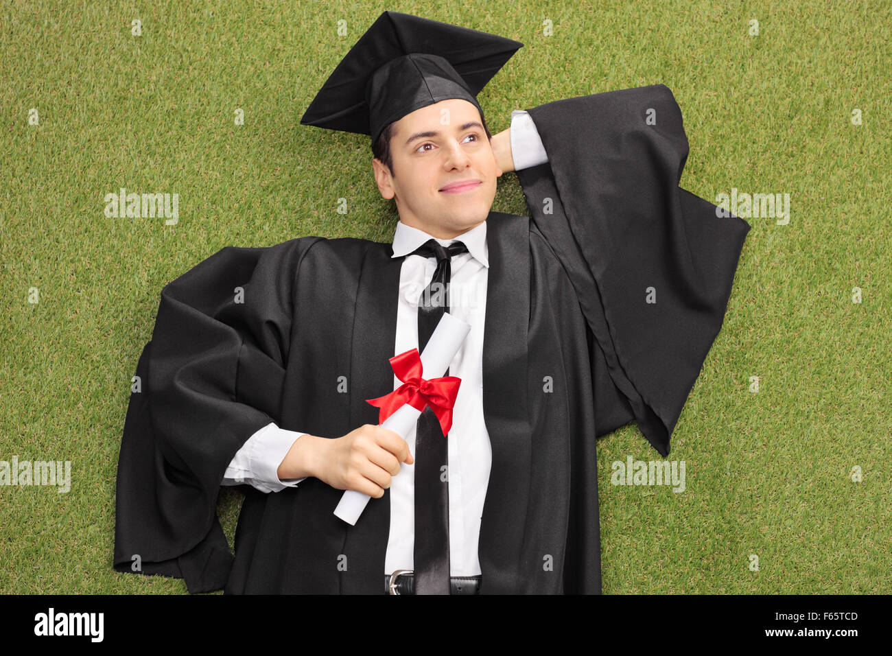 Young college graduate lying on grass with diploma in his hand and ...