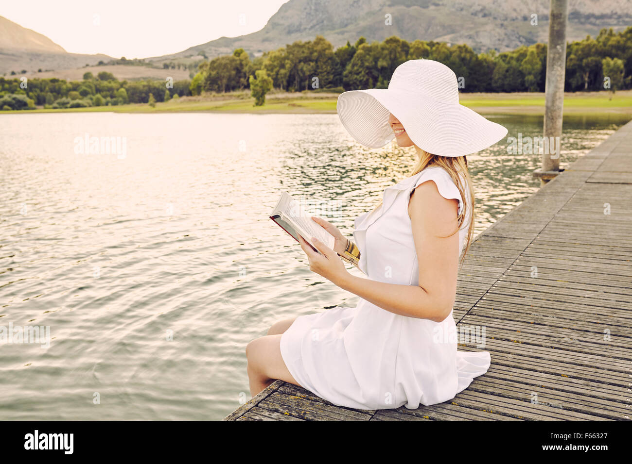 woman sitting at a dock reading a book Stock Photo - Alamy