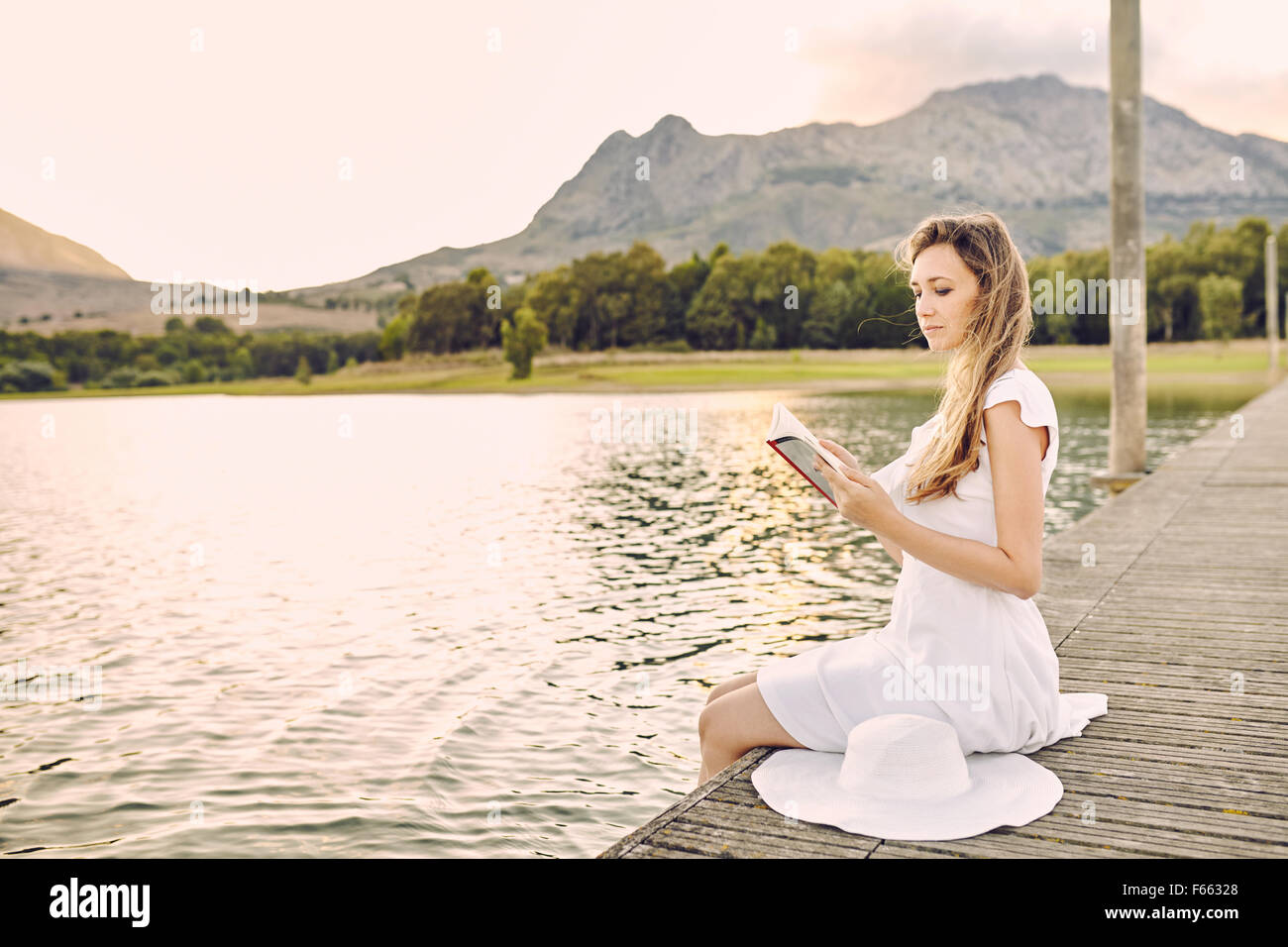 woman sitting at a dock reading a book Stock Photo - Alamy