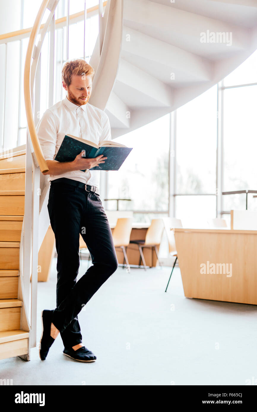 Handsome smart guy reading a book in a library Stock Photo - Alamy
