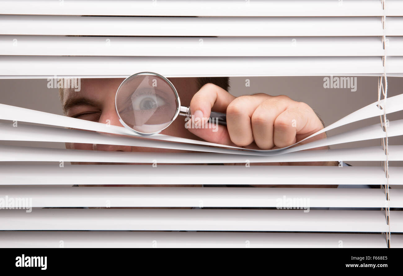 A young man looking through window blinds Stock Photo - Alamy