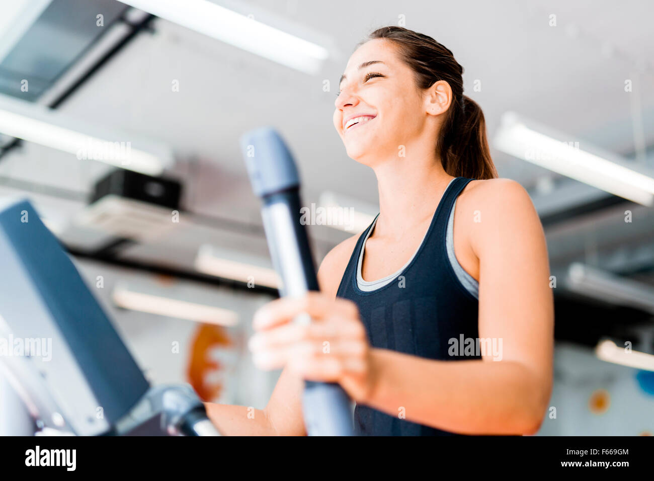 Beautiful young lady using the elliptical trainer in a gym in a ...