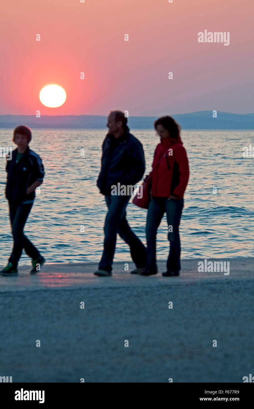 three people walk in sunset on the horizon above sea Stock Photo - Alamy