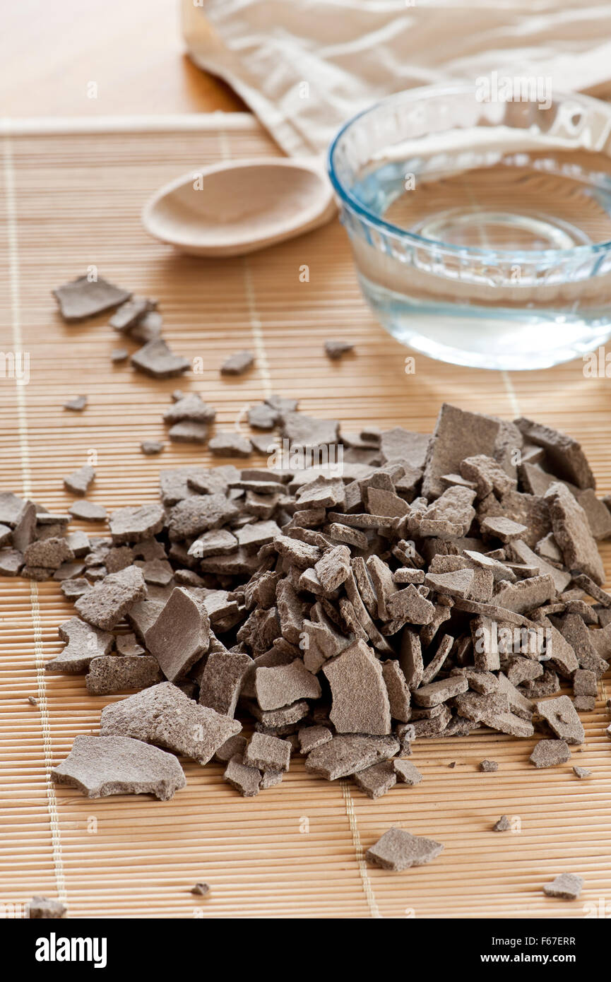 Ghassoul lava clay pieces, dried chips spilled out, glass bowl with ...