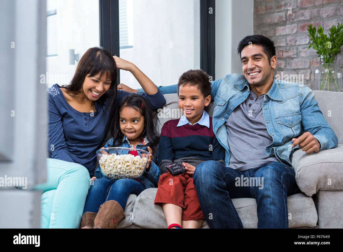 Happy young family eating popcorn while watching tv Stock Photo - Alamy