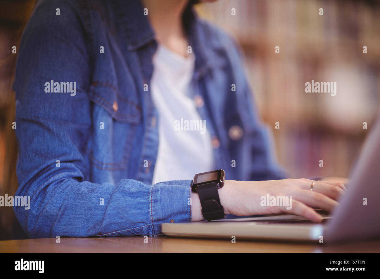 Student with smartwatch using laptop in library Stock Photo - Alamy