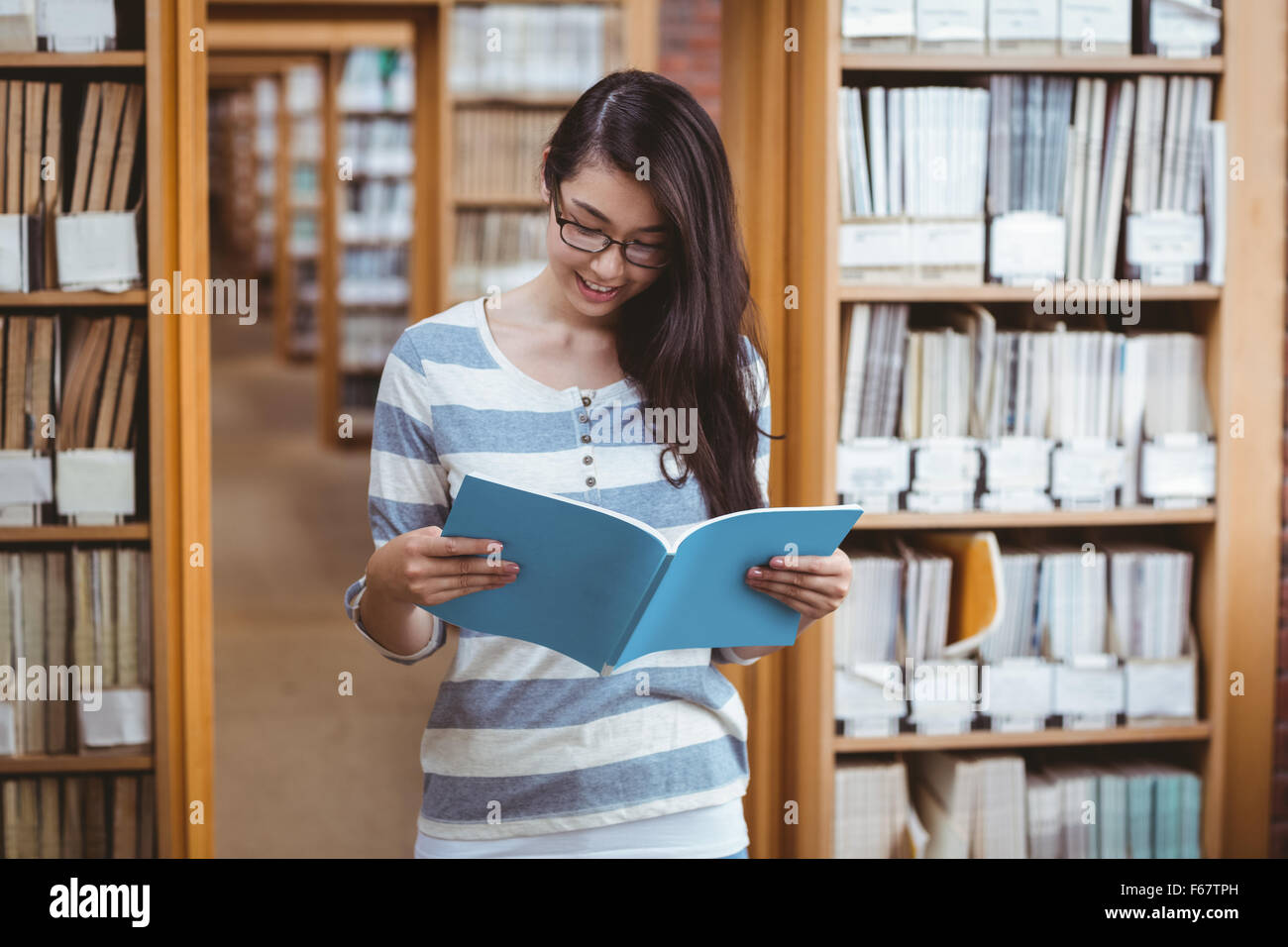 Pretty student reading a book in library Stock Photo - Alamy