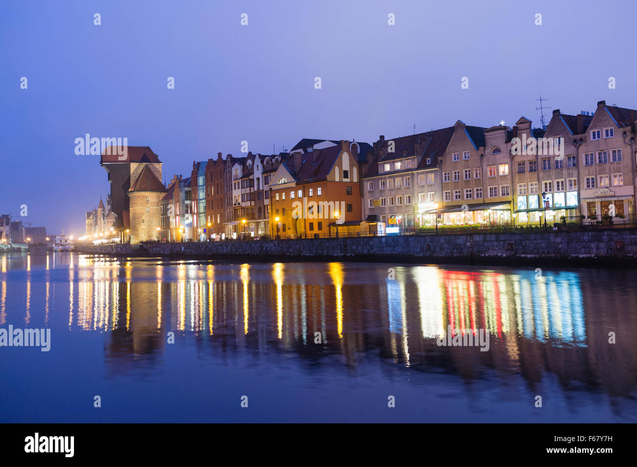 Waterfront tenements and crane reflected on Motlawa river at dusk ...