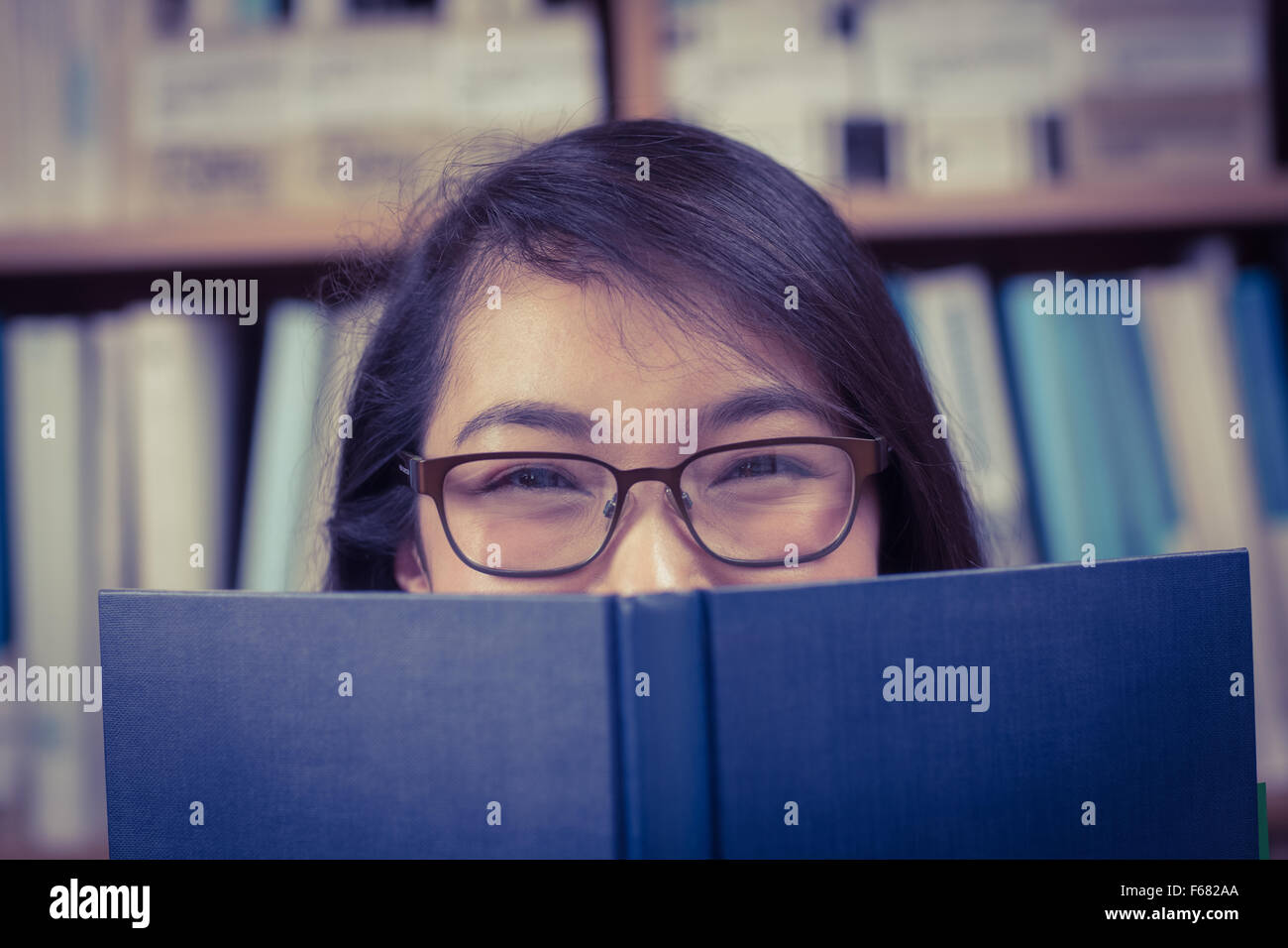 Pretty student hiding face behind a book Stock Photo - Alamy