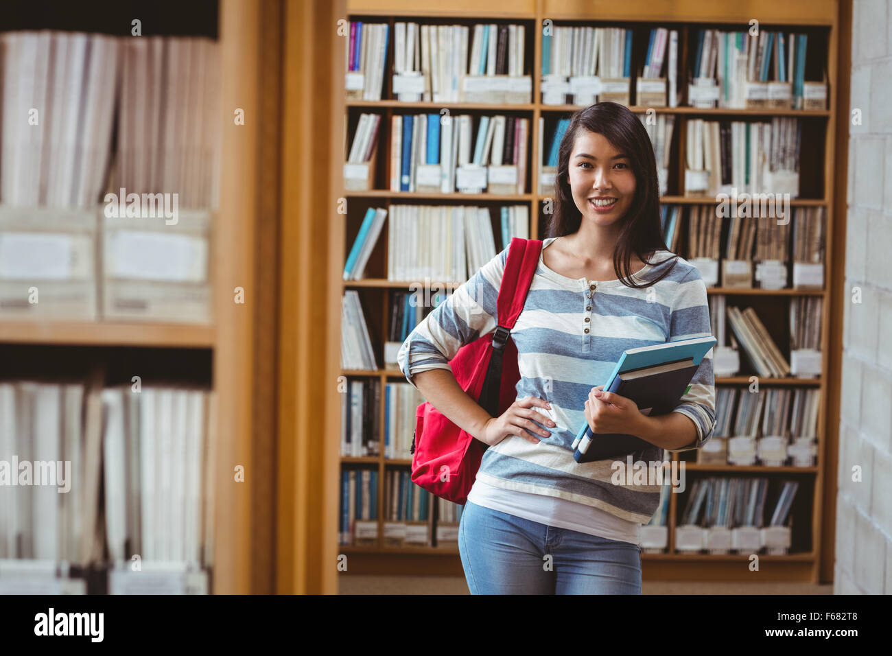 Pretty student standing in library holding a book Stock Photo - Alamy