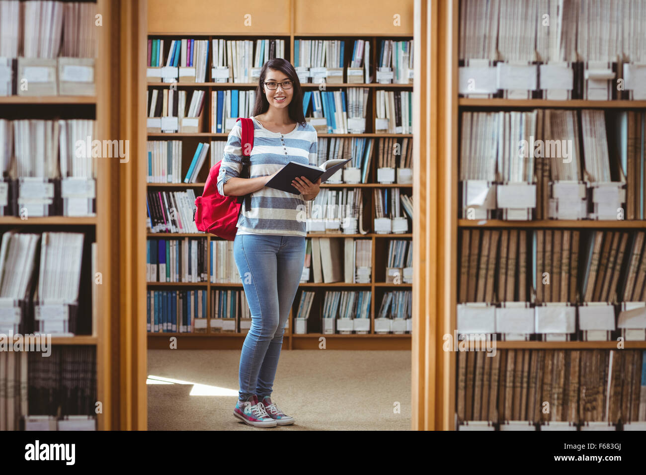 Pretty student with backpack reading a book in library Stock Photo - Alamy
