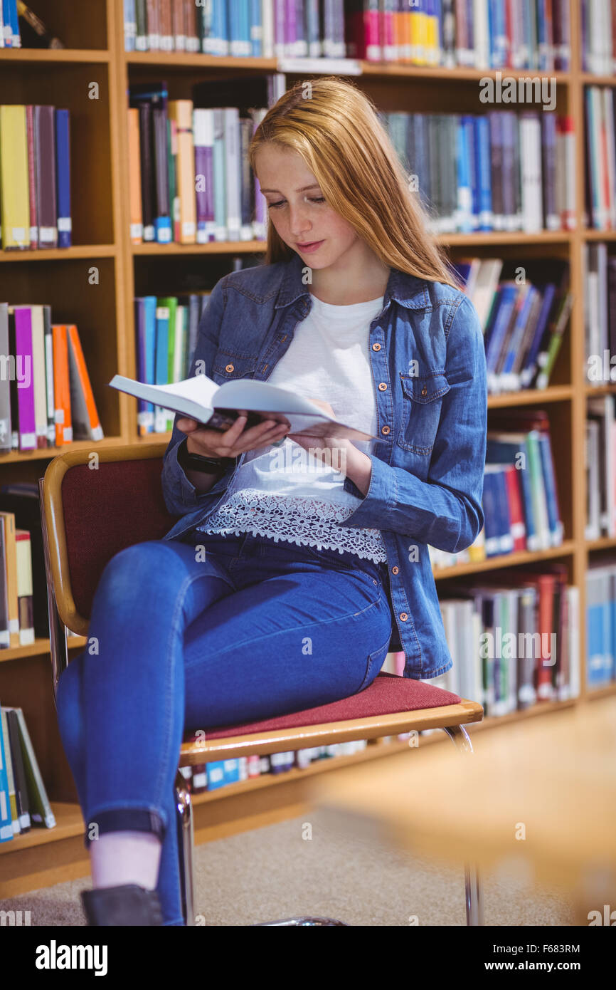 Pretty student sitting on chair reading book in library Stock Photo - Alamy