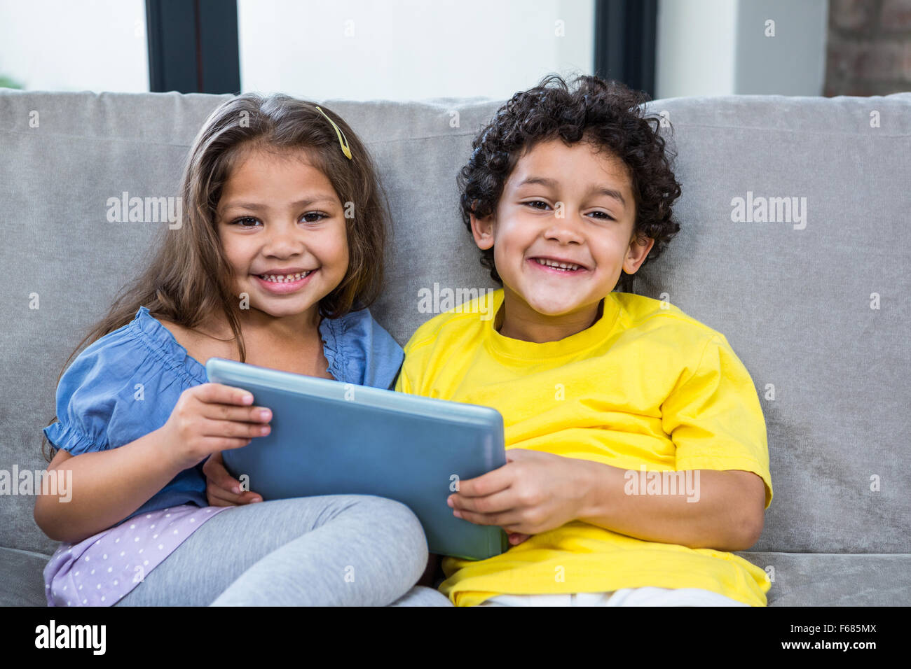 Smiling siblings using tablet on the sofa Stock Photo - Alamy