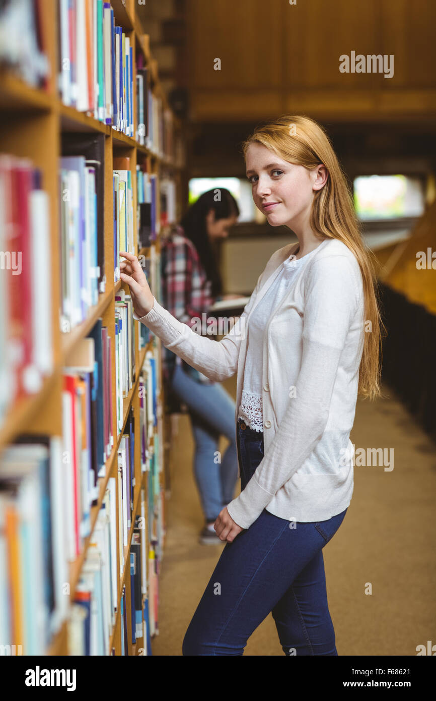 Blond student looking for book in library shelves Stock Photo - Alamy
