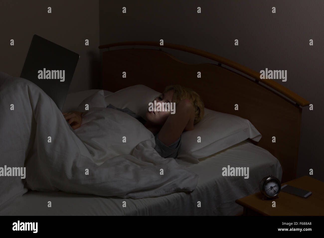 Teenage girl on laptop computer while in bed. Teen surrounded by ...