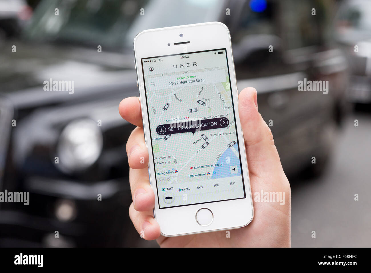Hand holding Apple iPhone using Uber app with black taxi behind, London ...
