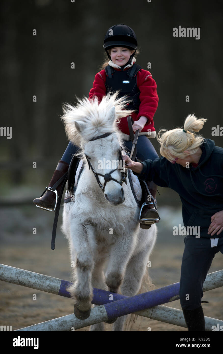 A young girl jumps a fence riding a pony in a stable yard in Hampshire ...