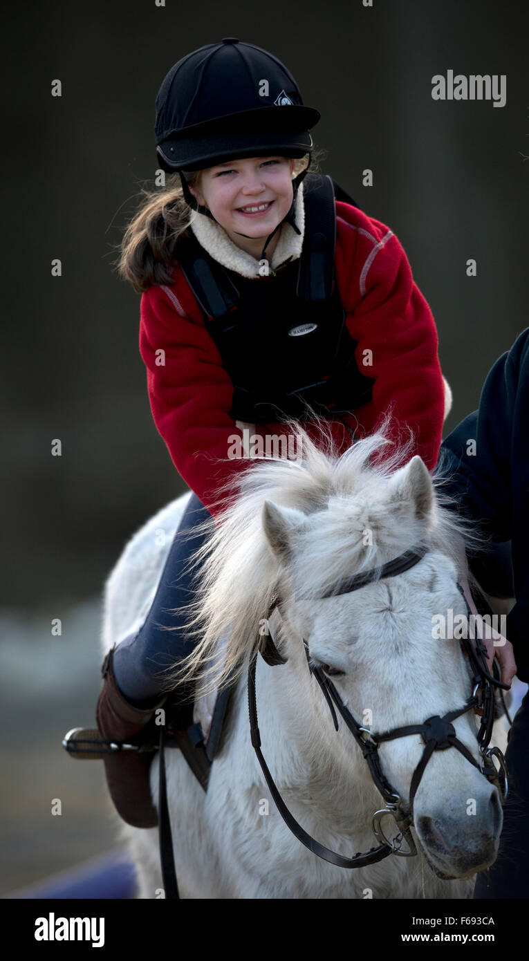A young girl jumps a fence riding a pony in a stable yard in Hampshire ...