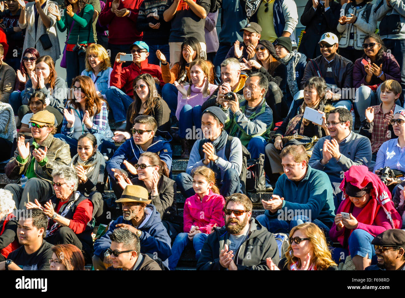 A large, diverse group of people sitting outside in rows as an audience ...