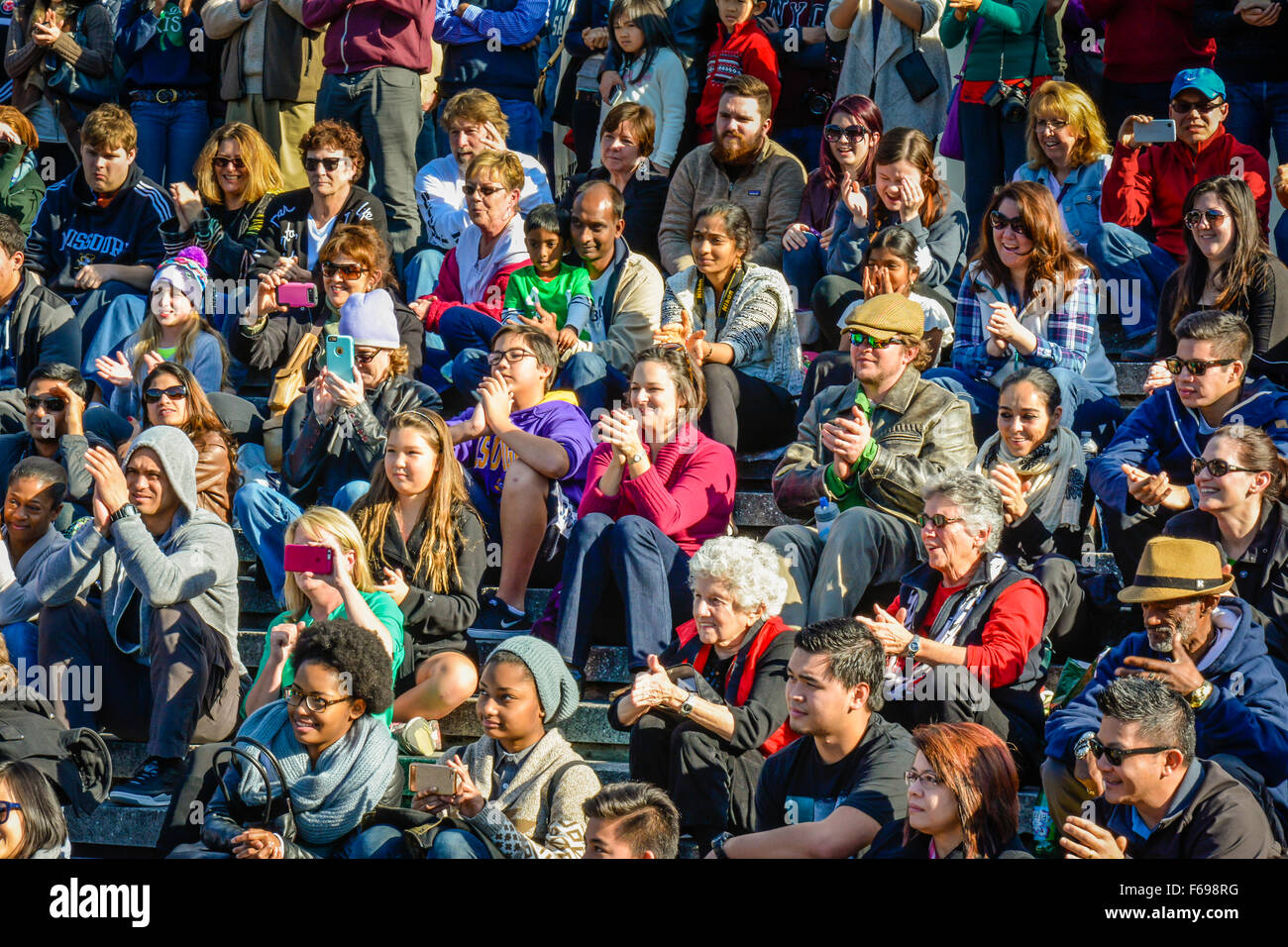 A large, diverse group of people sitting outside in rows as an audience ...