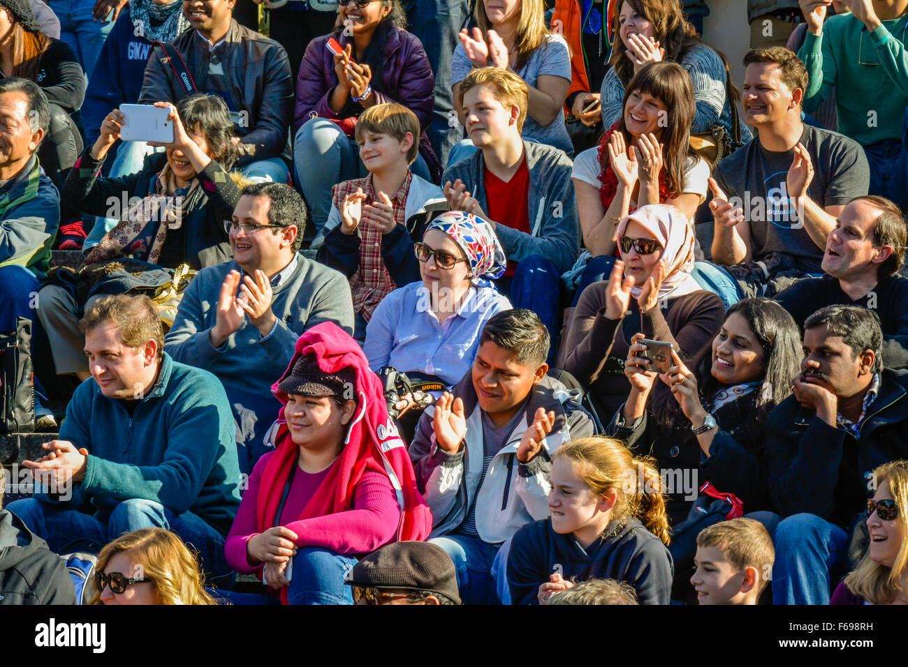 A large, diverse group of people sitting outside in rows as an audience ...