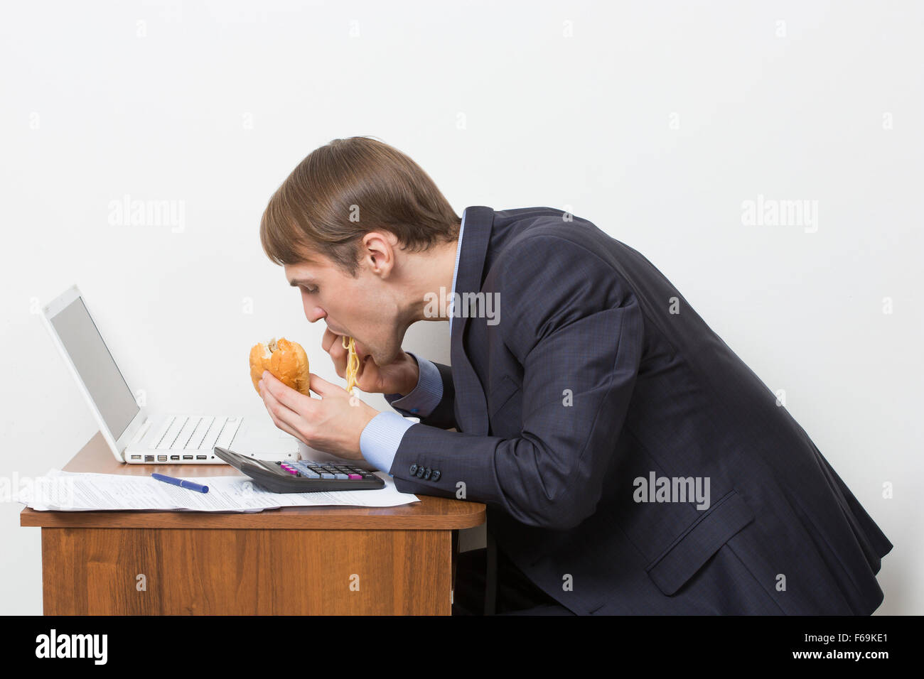 Man eating burger at desk Stock Photo - Alamy