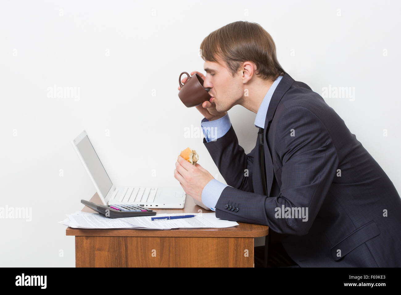 Man eating burger at desk Stock Photo - Alamy