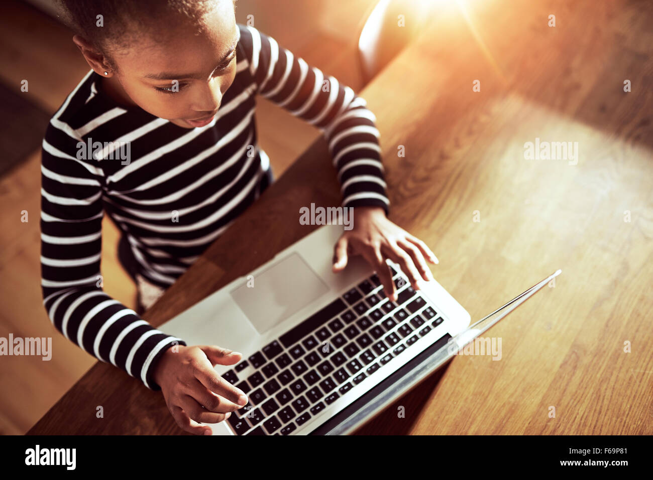 Young ethnic black girl sitting at the dining table at home typing on a ...