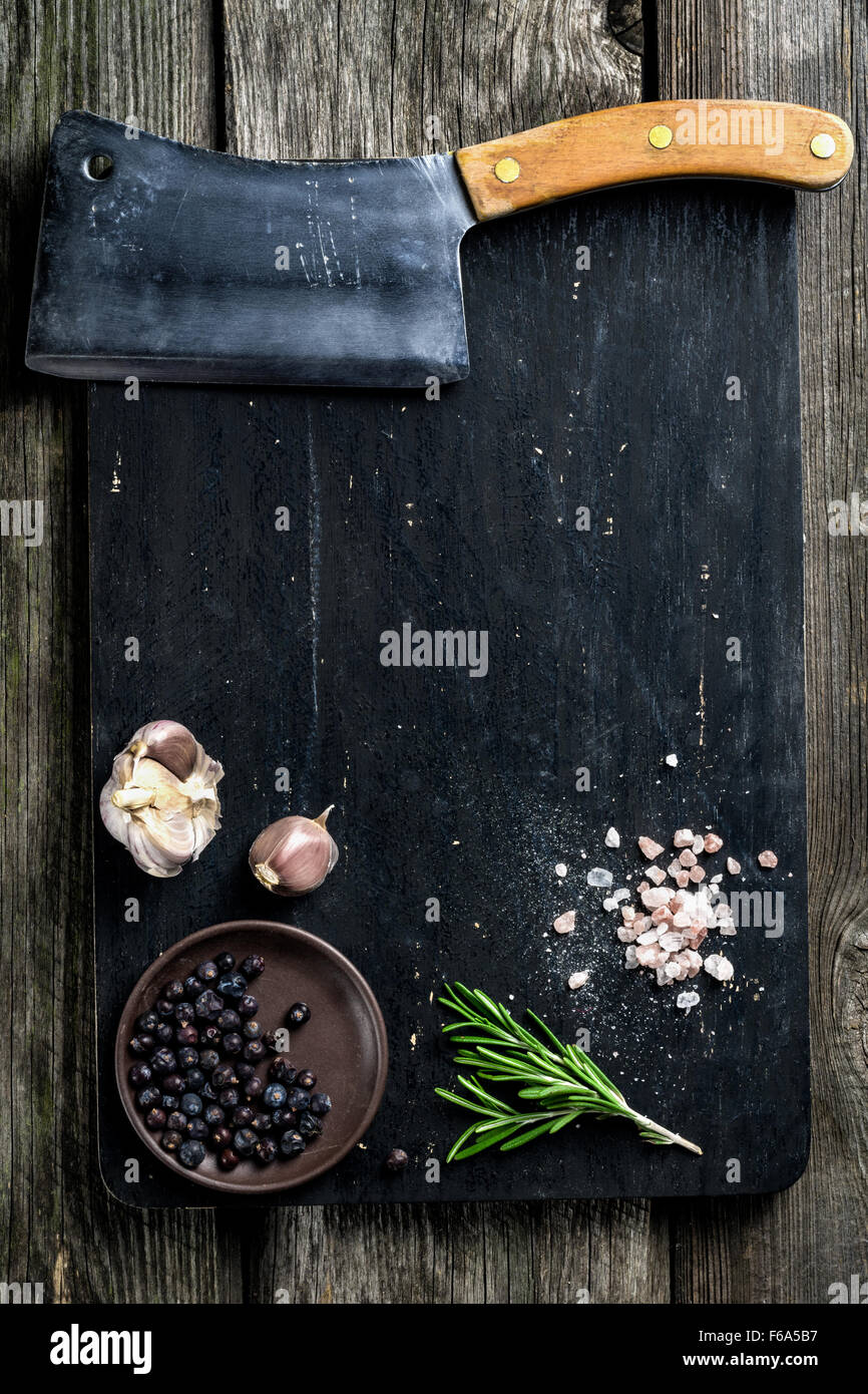 Cutting board, meat cleaver and condiments on dark wooden background ...