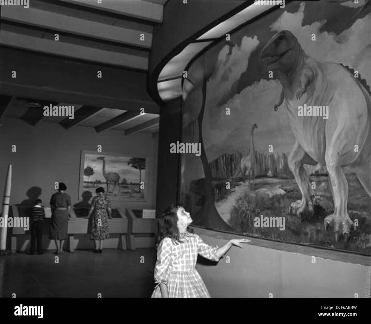 A historical image showing individuals viewing a painting of a dinosaur ...