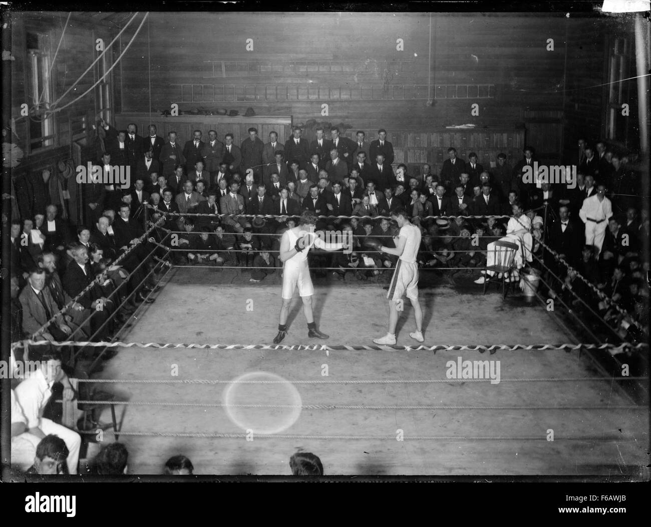 This image captures a boxing match with a crowd of male spectators ...