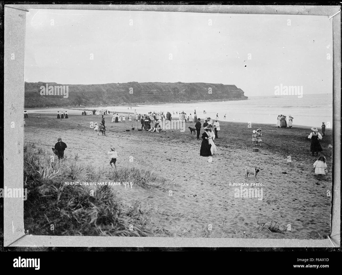 This historical photograph shows a crowd of people gathered at Opunake ...