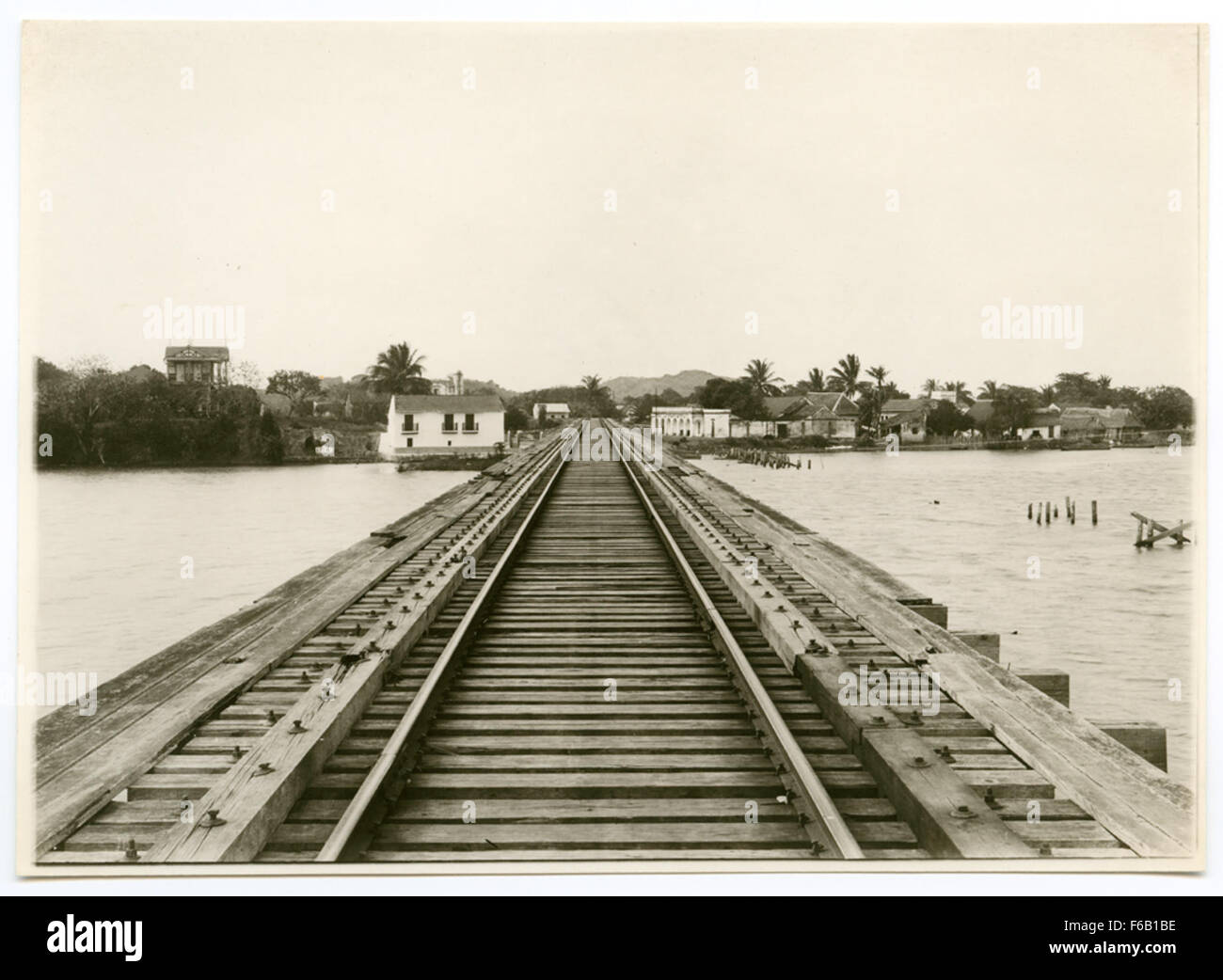 This image depicts railroad tracks crossing over water, with a village ...