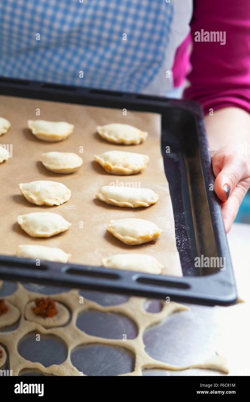 A woman holding a baking tray of uncooked pastry parcels, filled with ...