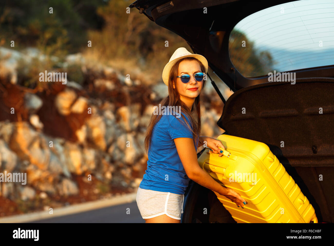 Young woman loading luggage into the back of car parked alongside the ...