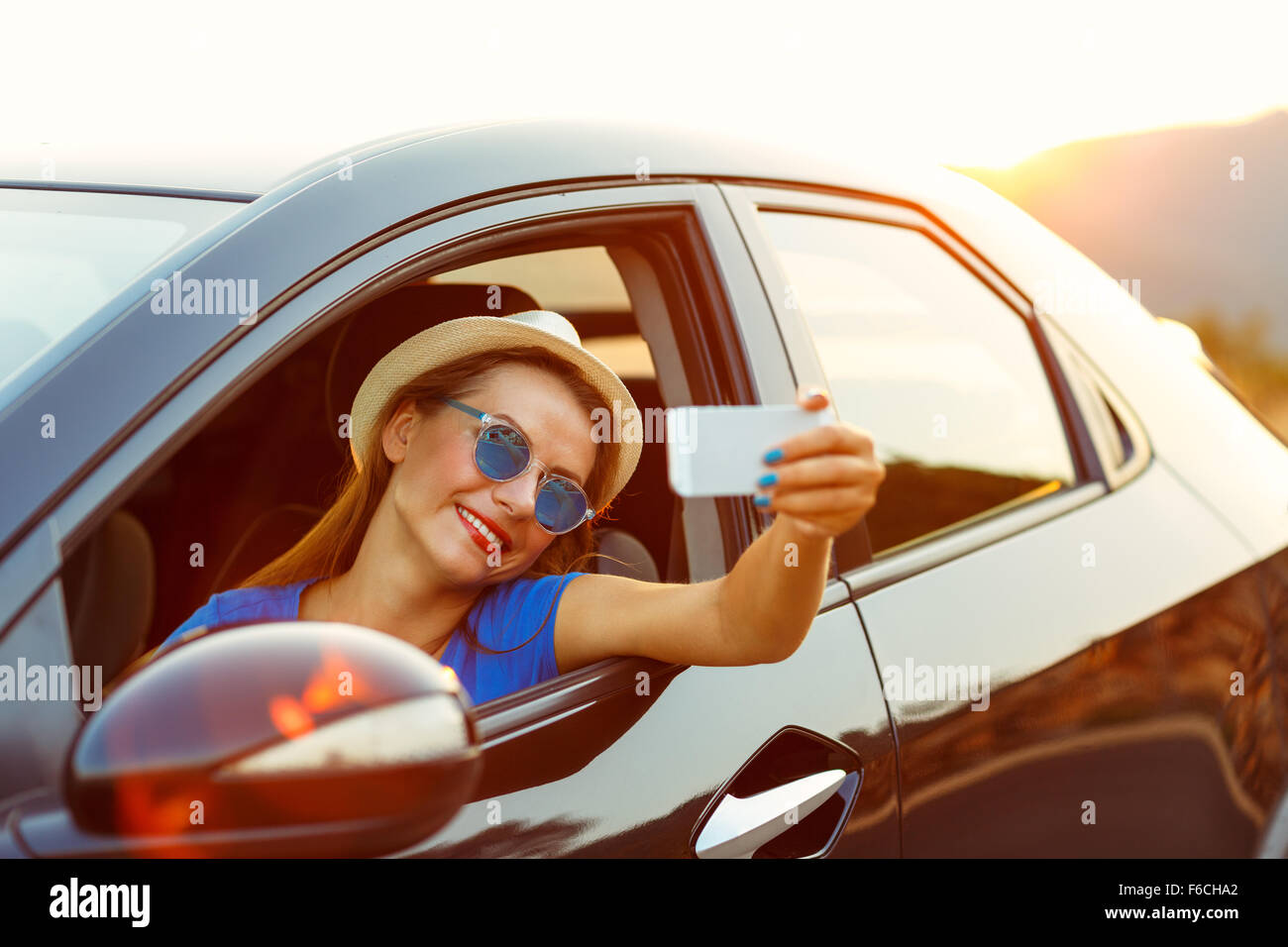 Young smiling woman in hat and sunglasses making self portrait sitting ...